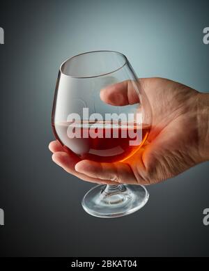 glass of cognac in human hand on grey background Stock Photo - Alamy