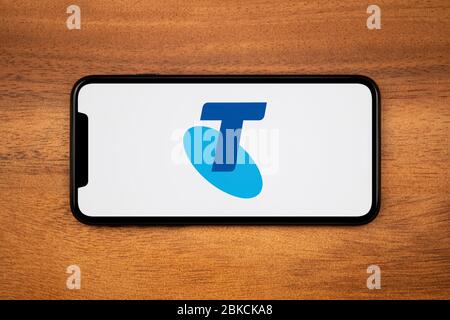 A smartphone showing the Telstra logo rests on a yellow background ...