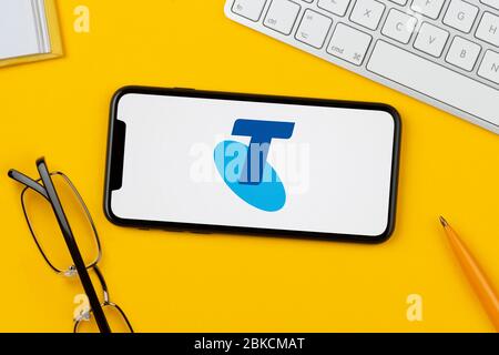 A smartphone showing the Telstra logo rests on a plain wooden table ...