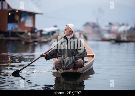 A Kashmiri man rowing shikara boat standing up after buying vegetables ...