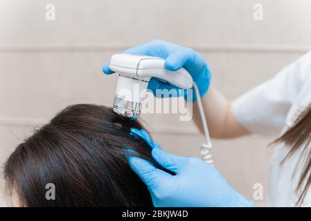 Trichoscopy of hair and scalp closeup. Trichoscope in the hands of a ...
