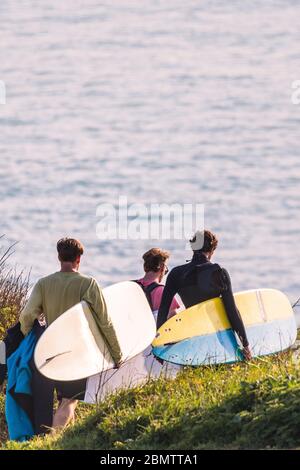 Walking group of friends carrying surfboards on sandy beach, with rocks ...