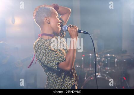 Side view of young female singer with Afro hairstyle standing against ...