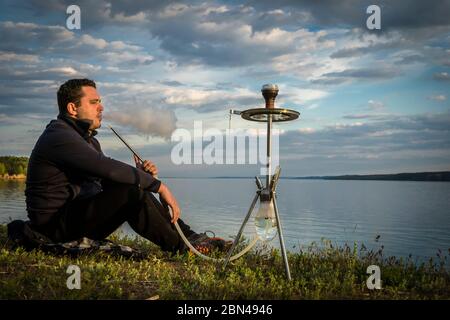 Man smoking hookah near the river at sunset Stock Photo - Alamy