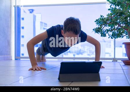 Kid with tablet computer doing push-ups sport exercises on balcony ...