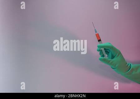 Beautiful hand holding creative syringe with red vaccine in the neon ...