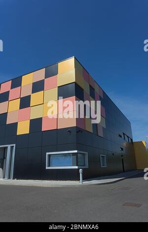Matt black cubic building with yellow and red tiles in one corner as ...