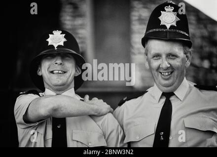 Two male police constables posing for a laugh with the wrong size ...