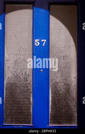 House number 57 on a royal blue wooden front door with dirty window ...