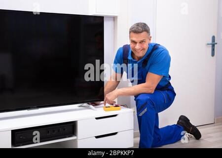 happy handyman holding digital multimeter and sitting on ladder near ...