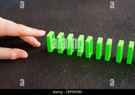 Hand ready to push domino piece to cause chain reaction. Row of green ...