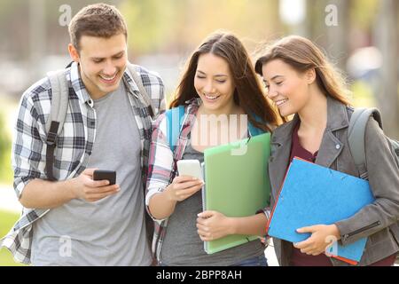 Three happy students checking smart phones outdoors in an university ...