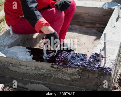 Woman hand with a brush covers the strip foundation with bituminous ...