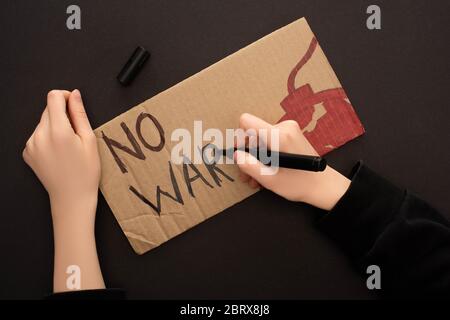 cropped view of woman drawing placard with no war lettering on black ...