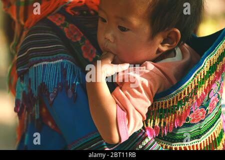 Hmong tribe child carrying a baby in a sling in a village on the Mekong ...