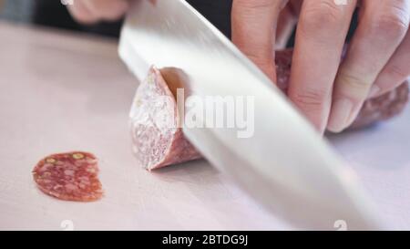 Slicing salami into thin rings ona white cutting board Stock Photo - Alamy