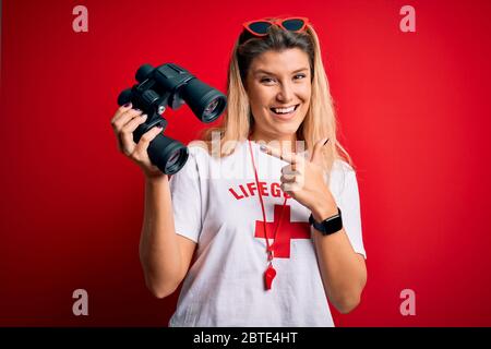 Young beautiful blonde lifeguard woman using binoculars and whistle ...