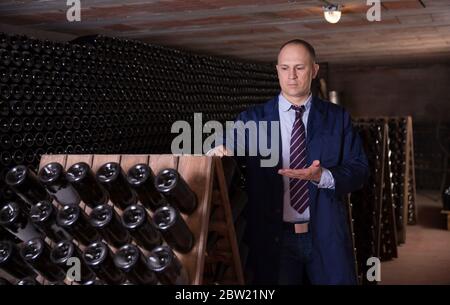 Male winemaker giving tour around winery, showing wine cellar with wine ...