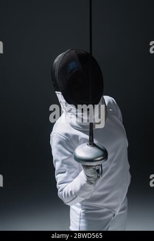 Fencer in fencing mask holding rapier and jumping on black background ...