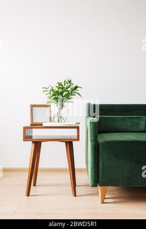 Table with frame, books and sofa near light wall Stock Photo - Alamy
