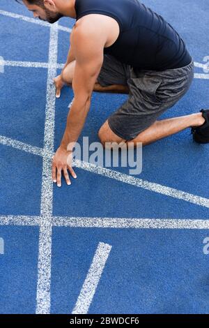cropped view of runner in start position on running track at stadium ...