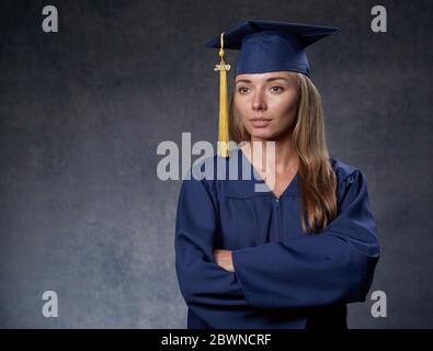 Beautiful blonde woman wearing graduation cap and ceremony robe holding ...