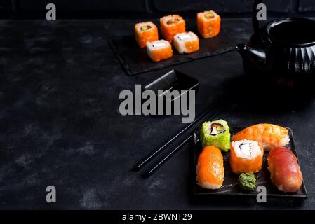 Asian food background with black iron teapot and sushi set on slate ...