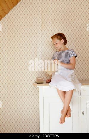 Girl sitting on chest of drawers at home Stock Photo - Alamy