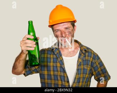 Thirsty and tired builder in safety helmet feels exhausted and holds bottle of brandy alcohol ...