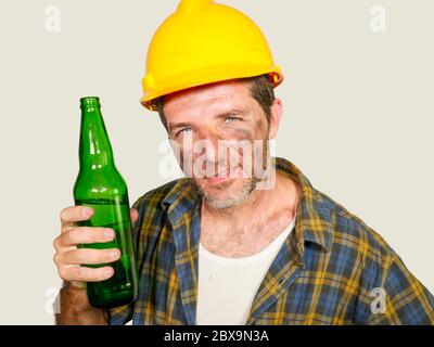 Thirsty and tired builder in safety helmet feels exhausted and holds bottle of brandy alcohol ...