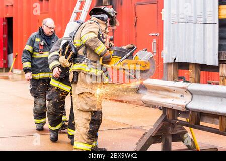 A firefighter using a saw to cut into a metal wall to gain access to a ...