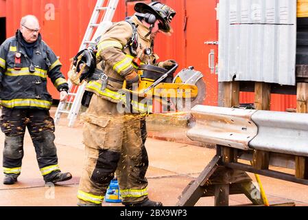 A firefighter using a saw to cut into a metal wall to gain access to a ...