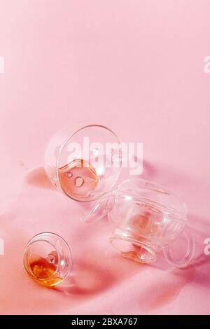 thrown glass teapot and spilled tea on a pink background. abstract ...