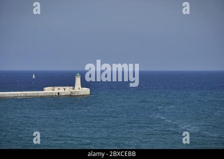 A lighthouse in the middle of a sea under a pink and blue clouded sky ...