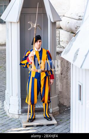 A Pontifical Swiss Guards stand by the Vatican Bronze door half closed ...