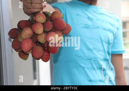 Fresh lychee fruits in white ribbed bowl with green leaves on textured ...