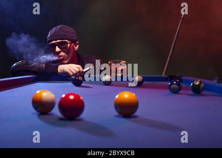 Man playing pool in a club smoking a cigarette Stock Photo - Alamy