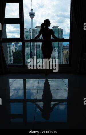 A slender girl is looking at the city through a large window. High ...