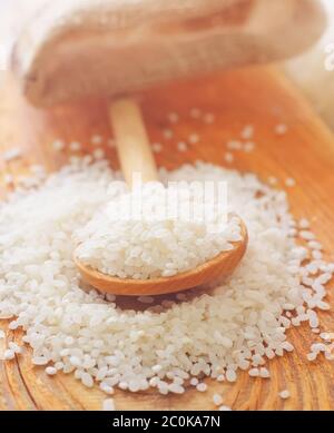 Raw rice in bowl, spoon and burlap fabric on wooden table, flat lay ...