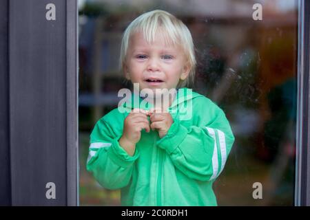 Toddle boy, crying heavily, standing in front of the door, looking at ...