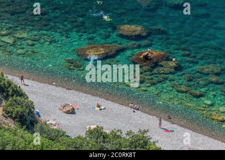 People sunbathe and swim on the pebble beach. Untouched nature, clean ...