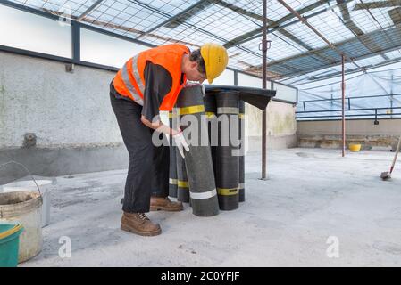Roofer installing rolls of bituminous waterproofing membrane for the waterproofing of a terrace ...