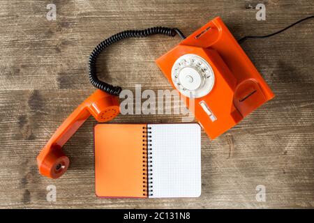 Vintage orange telephone and blank notebook on blue background, top ...