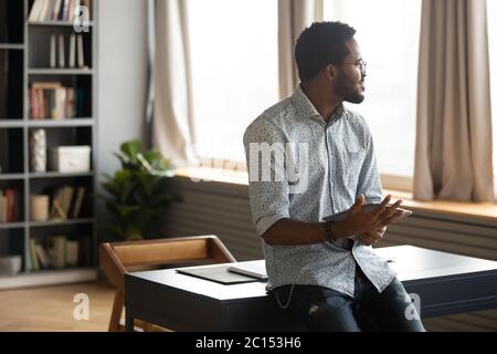 distracted african american freelancer looking away near laptop and cup ...