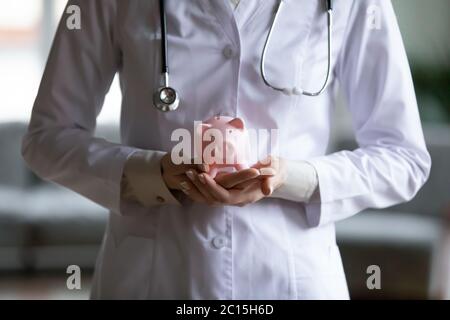 Doctor with pink piggy bank on blue background, close up Stock Photo ...