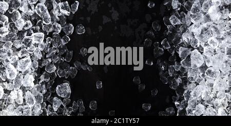 Pieces of crushed ice on black background, top view. Space for text ...