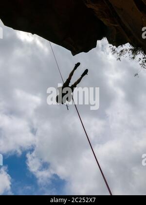 Abseiling a negative sanstone rock wall with blue sky on background ...