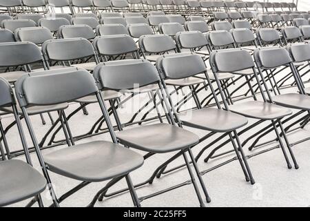 rows of empty black folding chairs in a large event hall with dark ...