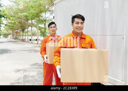 Delivery service workers wearing orange uniform clothes carrying boxes ...