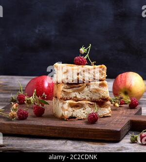 square pieces of apple pie are stacked on a brown wooden board, sponge ...